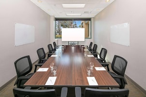 Uma sala de conferência com uma mesa comprida, cadeiras pretas e dois quadros brancos nas paredes.
