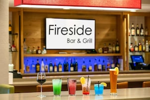 Uma área de bar com um letreiro que diz 'Fireside Bar & Grill' e diversos drinques coloridos no balcão.