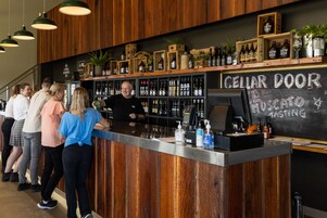 Uma área de bar com balcão de madeira, prateleiras com garrafas e um quadro negro com a inscrição 'CELLAR DOOR'.