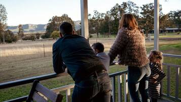 Uma família numa varanda com vista para um campo gramado, árvores e colinas ao longe.