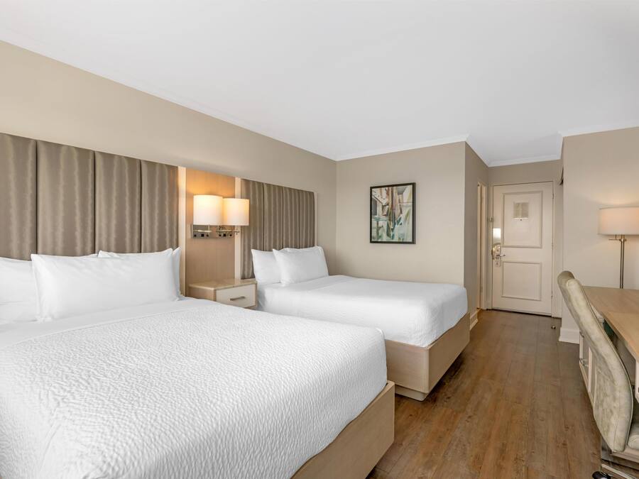 Quarto de hotel com duas camas, uma escrivaninha, uma cadeira, uma televisão e uma porta.