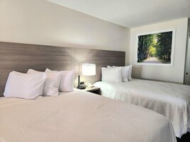 Quarto de hotel com duas camas, uma mesa de cabeceira com abajur, um telefone e um quadro de uma floresta na parede.