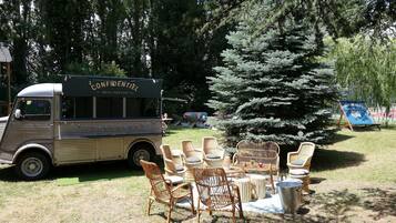 Um food truck antigo chamado 'Confidentiel', com móveis de vime e uma grande árvore de Natal em um parque.