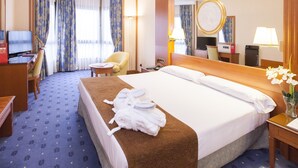 Quarto de hotel com uma cama grande, uma escrivaninha com computador, uma cadeira, televisão e espelho de banheiro.