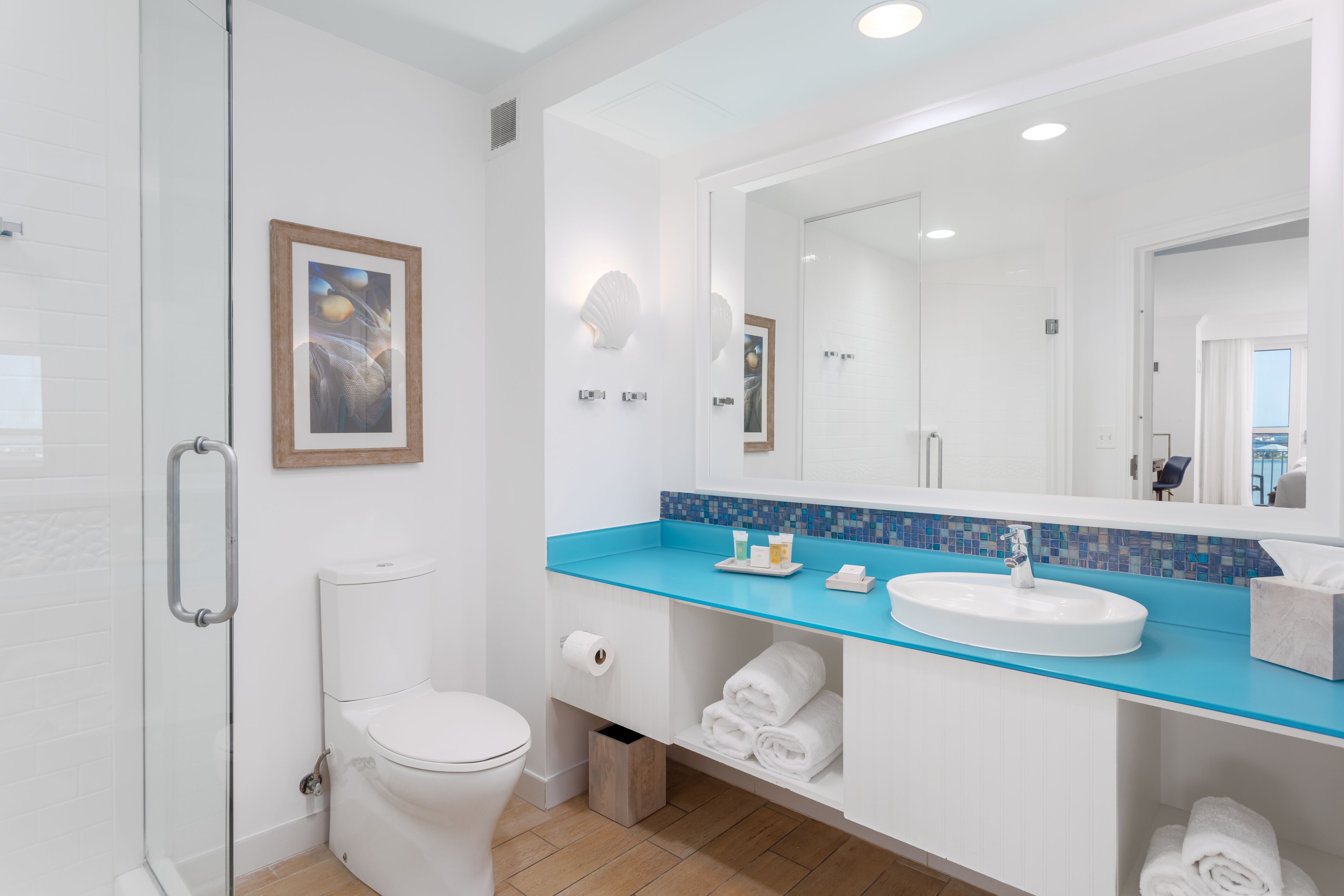 Casa de banho moderna com cabine de chuveiro em vidro, sanita branca, espelho grande e bancada azul.