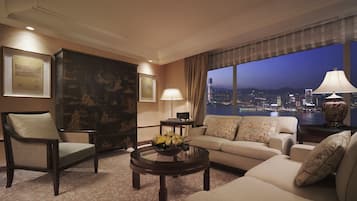 Uma sala de estar moderna com sofá, poltronas, mesa de centro e vista para um horizonte urbano noturno.