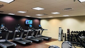 Uma academia com esteiras, televisão e equipamentos de musculação.