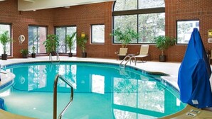 Piscina interior com água azul cristalina, cercada por paredes de tijolo e amplas janelas.