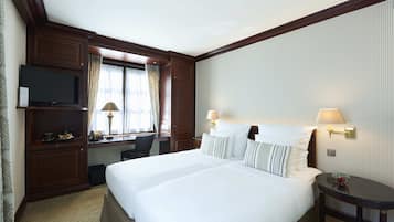 Quarto de hotel com duas camas, uma secretária com televisão e uma janela com cortinas.