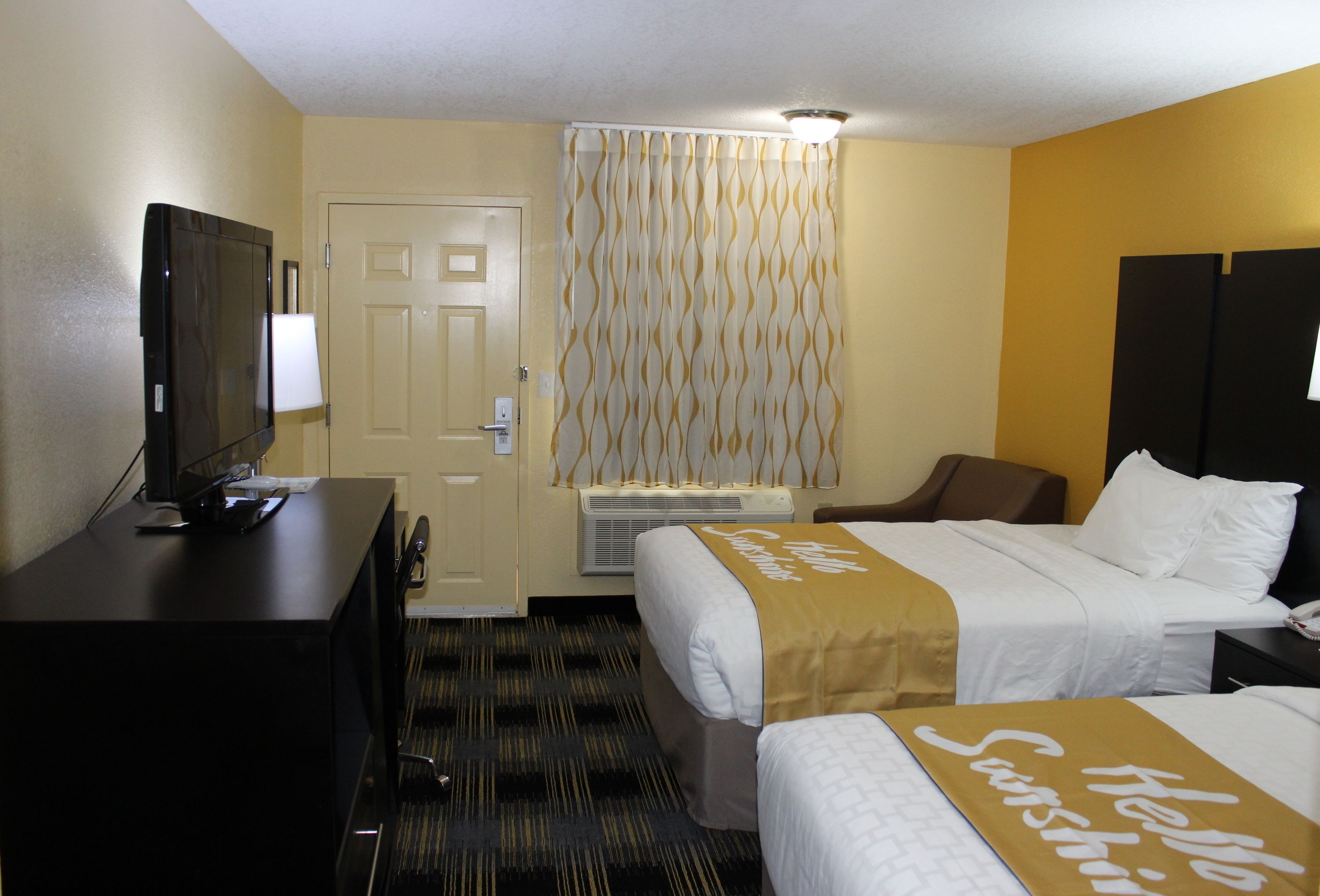 Quarto de hotel com duas camas, uma mesa, uma televisão e um ar condicionado.