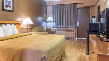 Quarto de hotel com uma cama, duas luminárias de cabeceira, uma televisão, uma janela com cortinas e um quadro na parede.