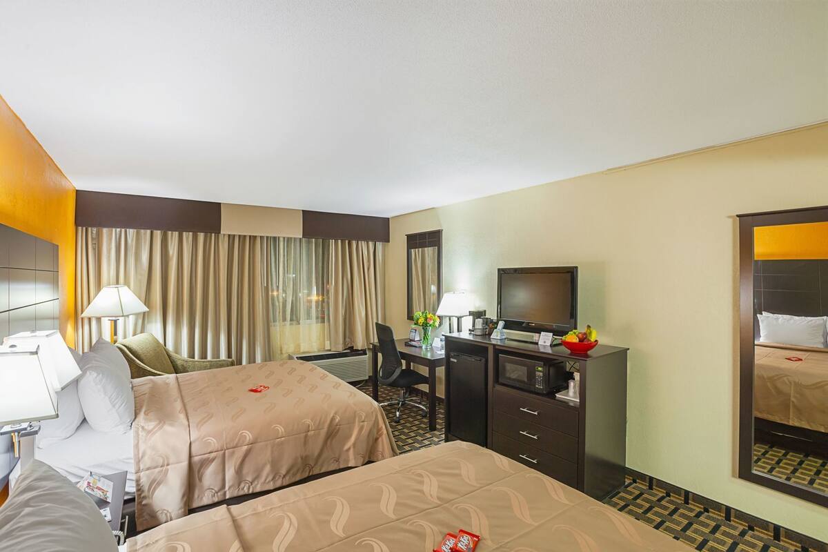 Quarto de hotel com duas camas, uma escrivaninha com computador, televisão e minibar.