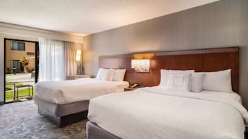 Quarto de hotel com duas camas, uma janela grande com cortinas, vista para o exterior e uma mesinha com abajur.