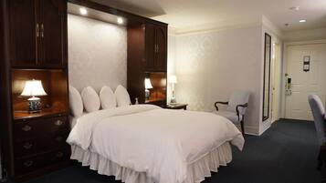 Quarto de hotel com uma cama grande, duas mesas de cabeceira com luminárias, uma cadeira e uma porta.