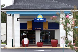 Um Days Inn by Wyndham com um letreiro 'Lobby', grandes vasos de plantas e um aviso de 'Estacionamento Apenas para Hóspedes Registrados'.