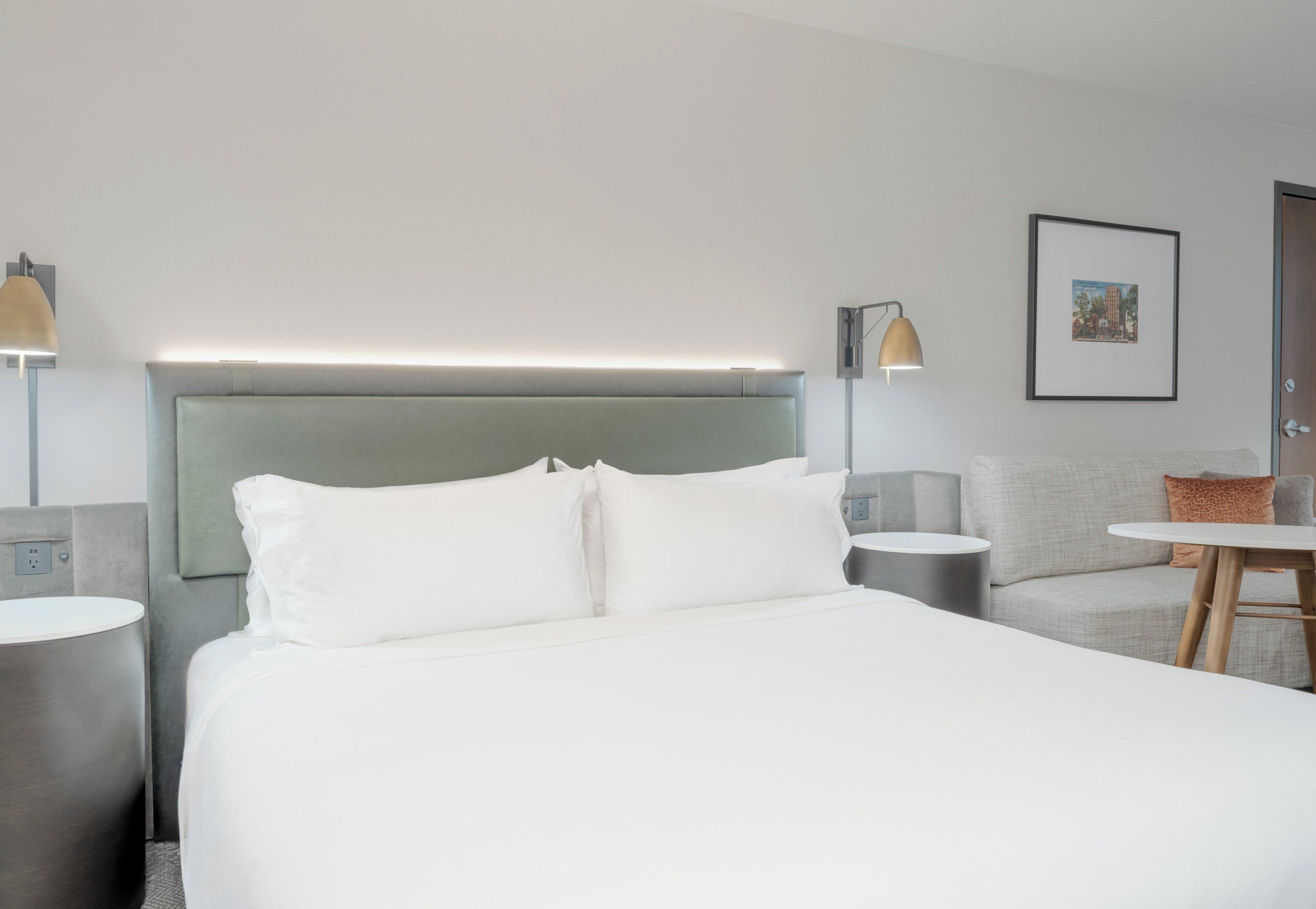 Quarto de hotel com uma cama grande, mesas de cabeceira, um sofá e uma pequena mesa.