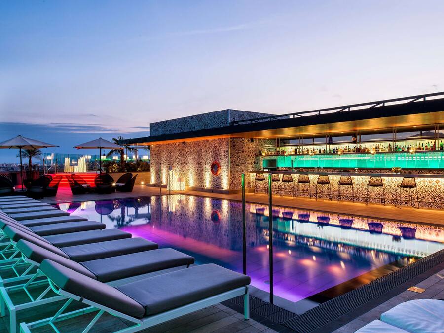 Uma área de piscina no terraço com espreguiçadeiras, bar e piscina com iluminação colorida.