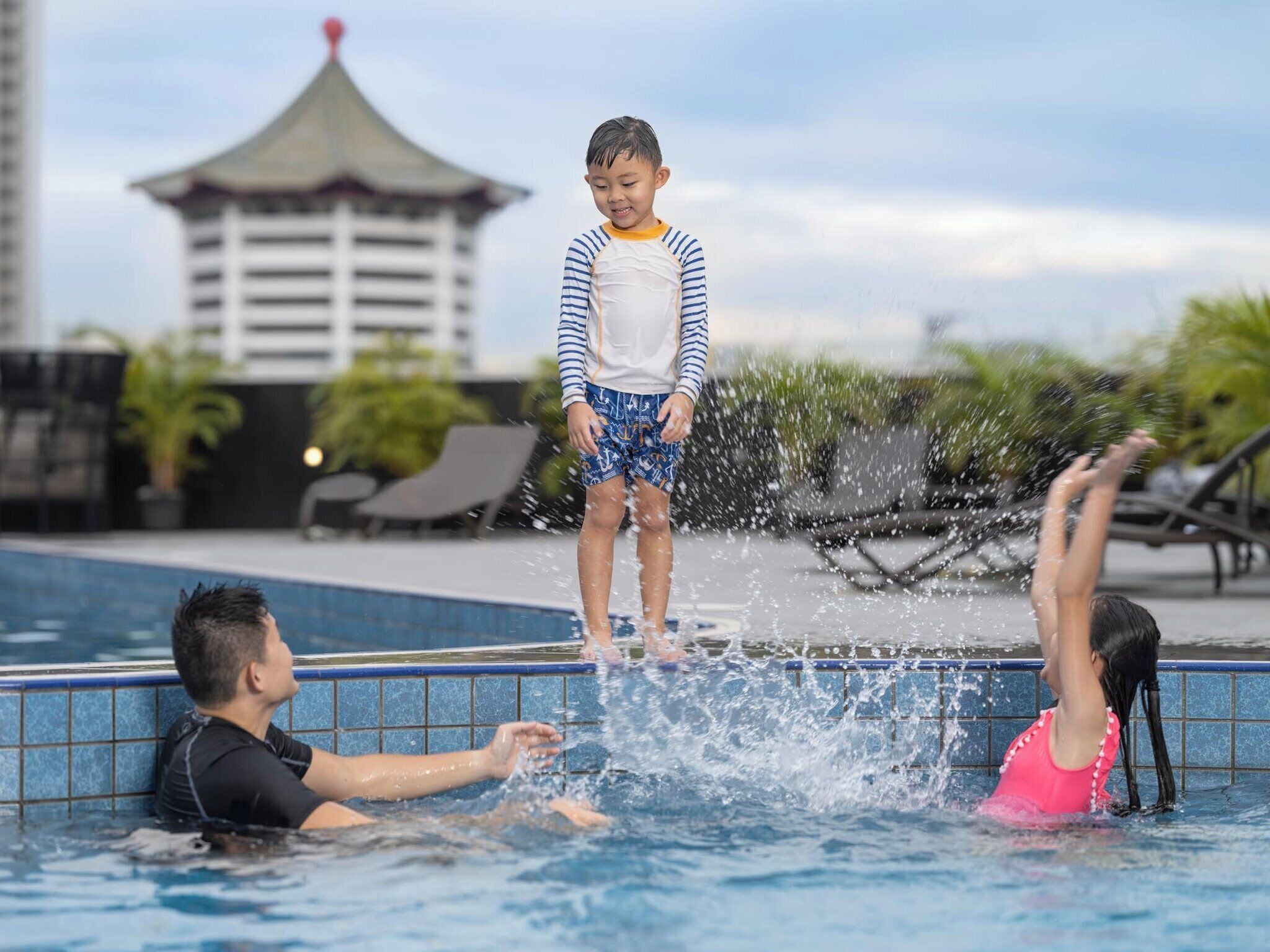 Piscina com uma criança na borda e adultos na água.
