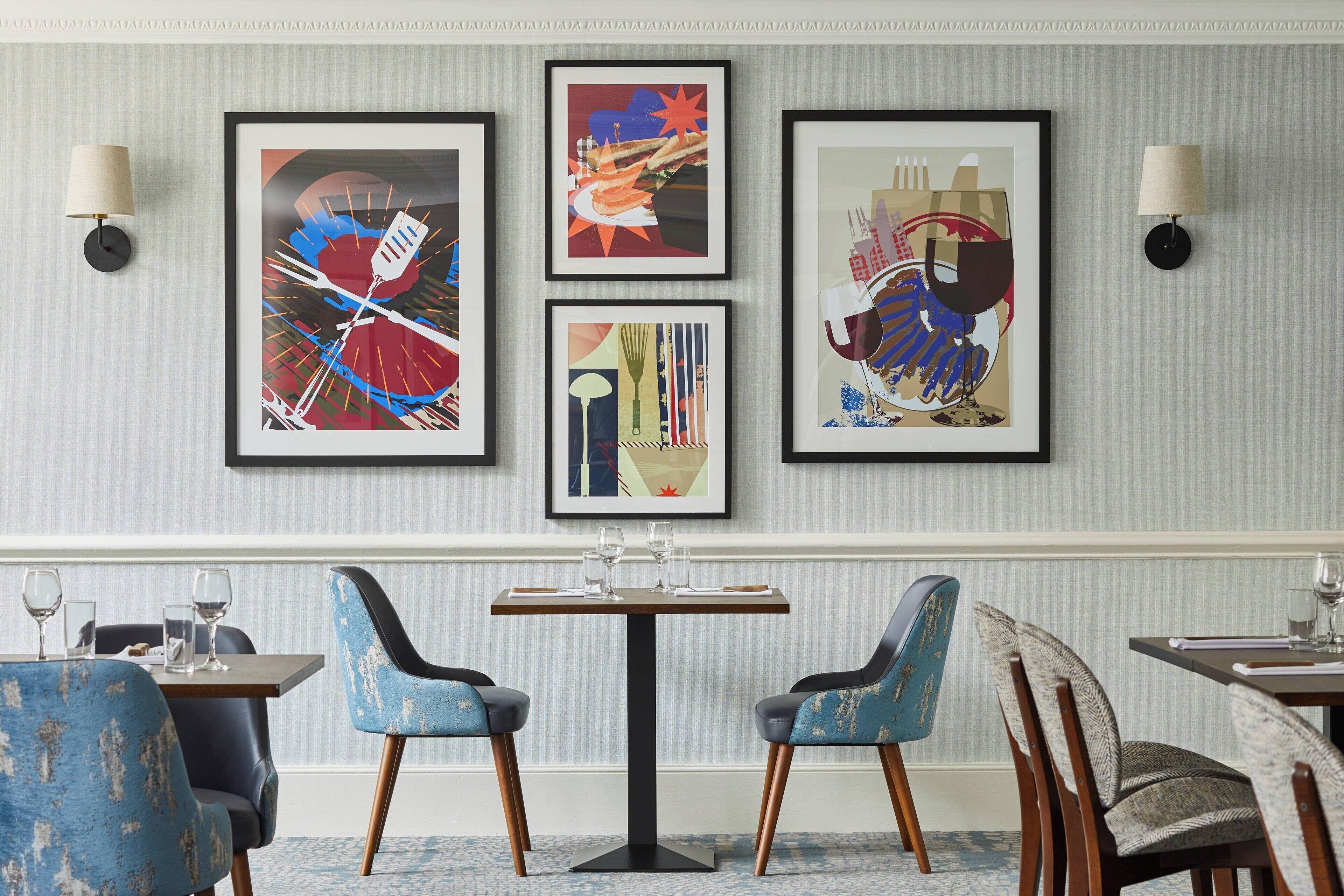 Uma área de jantar com mesa posta para dois, obras de arte na parede e cadeiras modernas.