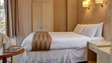 Quarto de hotel com cama, mesa de cabeceira, abajur e janela com cortinas.
