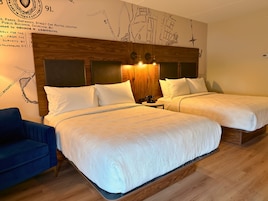 Quarto de hotel com duas camas, cabeceira de madeira, uma poltrona azul e um mapa na parede.