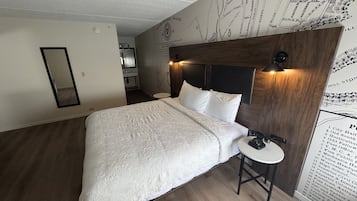 Quarto de hotel com uma cama grande, mesa de cabeceira com abajur e parede com mapa.