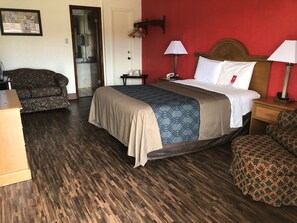 Quarto de hotel com cama, duas mesas de cabeceira, cómoda de madeira, sofá e espelho.