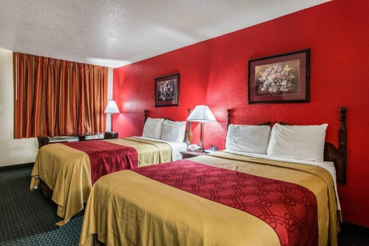 Quarto de hotel com duas camas, paredes vermelhas e duas luminárias.