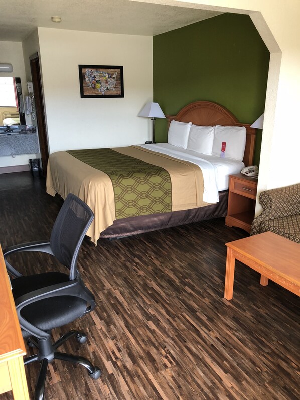 Quarto de hotel com cama, escrivaninha, cadeira, mesa de cabeceira e abajur.