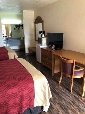 Quarto de hotel com duas camas, uma escrivaninha com televisão, máquina de café e lata de lixo.
