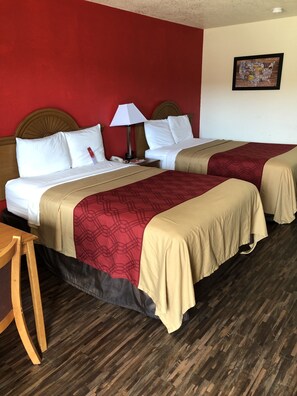 Quarto de hotel com duas camas, cabeceira de madeira, parede vermelha, soalho de madeira e uma pequena mesa.