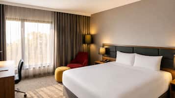 Quarto de hotel com uma cama grande, uma escrivaninha, uma cadeira e um abajur.