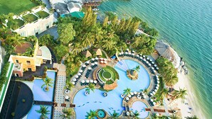 Vista aérea de um resort com várias piscinas, palmeiras e acesso à praia.