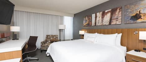 Quarto de hotel com cama, escrivaninha, cadeira e obras de arte na parede.