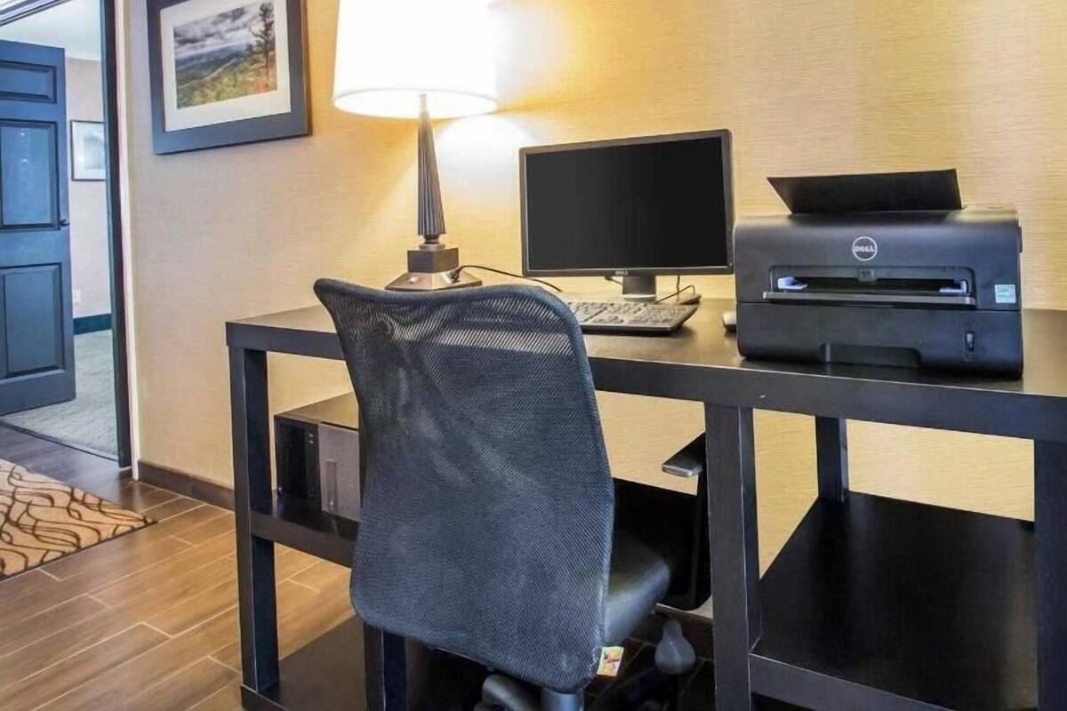 Quarto de hotel com escrivaninha, computador, impressora e luminária.