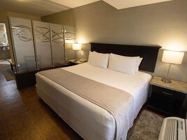 Quarto de hotel com uma cama grande, duas luminárias de cabeceira, mesas de cabeceira e um espelho com detalhes decorativos, além de piso coberto por carpete.