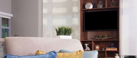 Uma sala de estar moderna com um sofá marrom, uma mesa de centro de vidro e uma TV sobre um suporte de madeira.