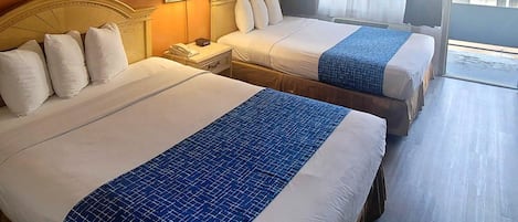 Quarto de hotel com duas camas, mesa de cabeceira com abajur, quadro na parede e janela com cortinas.