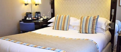 Quarto de hotel com uma cama grande, uma escrivaninha com cafeteira e uma cadeira.