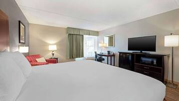 Quarto de hotel com uma cama grande, uma escrivaninha com televisão de tela plana, uma cadeira, um abajur, um sofá vermelho e uma janela com cortinas.