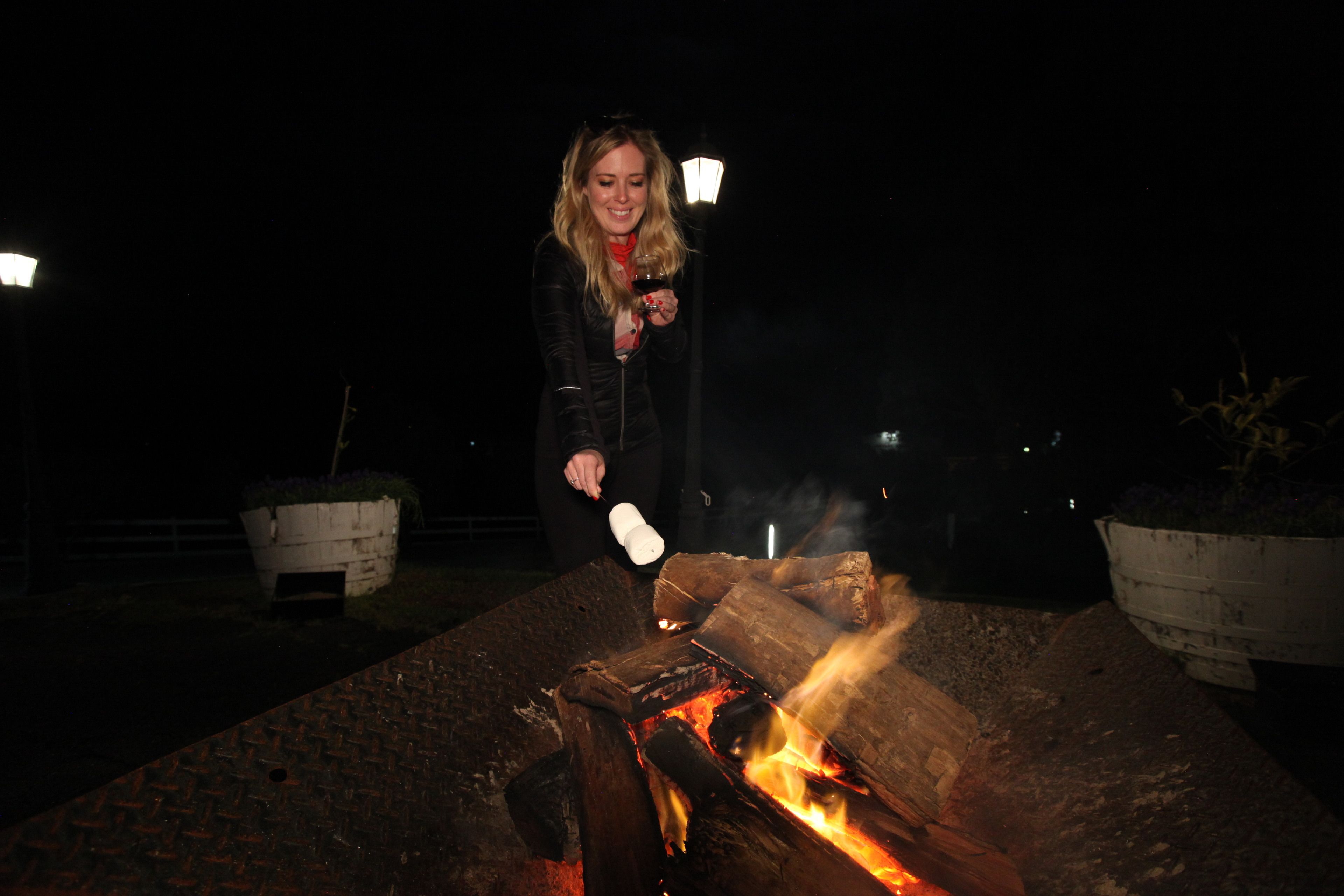 Alguém assando marshmallows sobre uma fogueira à noite.