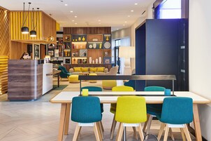 Espaço interior moderno com área de refeições, balcão de recepção e sala de estar com sofá e estantes.