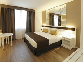 Quarto de hotel com cama grande, mesa de cabeceira e escrivaninha com cadeira.