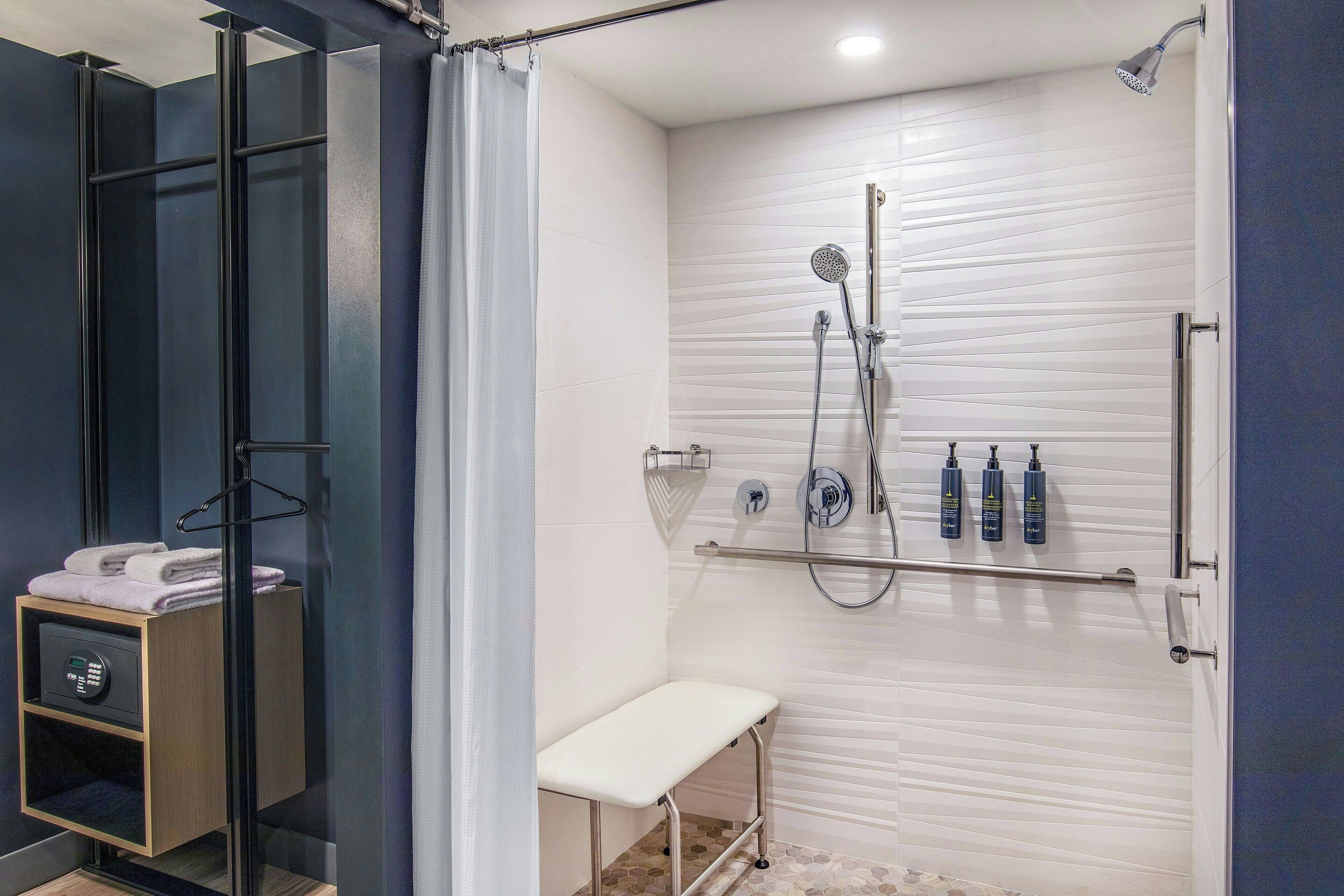 Uma casa de banho moderna com cabine de duche em vidro, um banco, porta-toalhas e um prateleira com artigos de higiene pessoal.