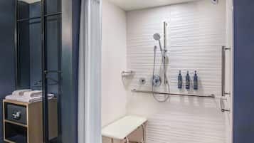 Uma casa de banho moderna com cabine de duche em vidro, um banco, porta-toalhas e um prateleira com artigos de higiene pessoal.