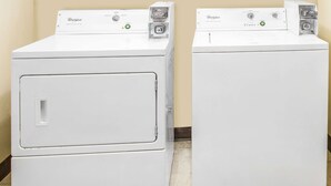 Duas máquinas de lavar roupa Whirlpool brancas, de abertura frontal, lado a lado numa divisão com chão em azulejos e parede lisa.