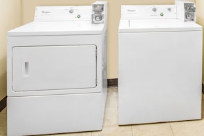 Duas máquinas de lavar roupa Whirlpool brancas, de abertura frontal, lado a lado numa divisão com chão em azulejos e parede lisa.