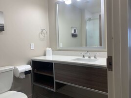 Um banheiro com pia branca, duas torneiras, um espelho grande, vaso sanitário com dispensador de papel toalha e porta-toalhas na parede.
