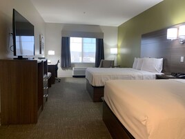 Quarto de hotel com duas camas, uma escrivaninha com cadeira, televisão e janela com cortinas.