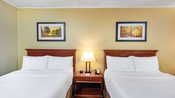 Quarto de hotel com duas camas, uma mesa de cabeceira com abajur, e duas quadros na parede.